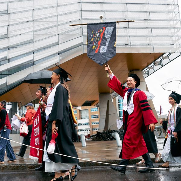 A color photo showing people walking to Cornell University graduation behind the Cornell Bowers flag